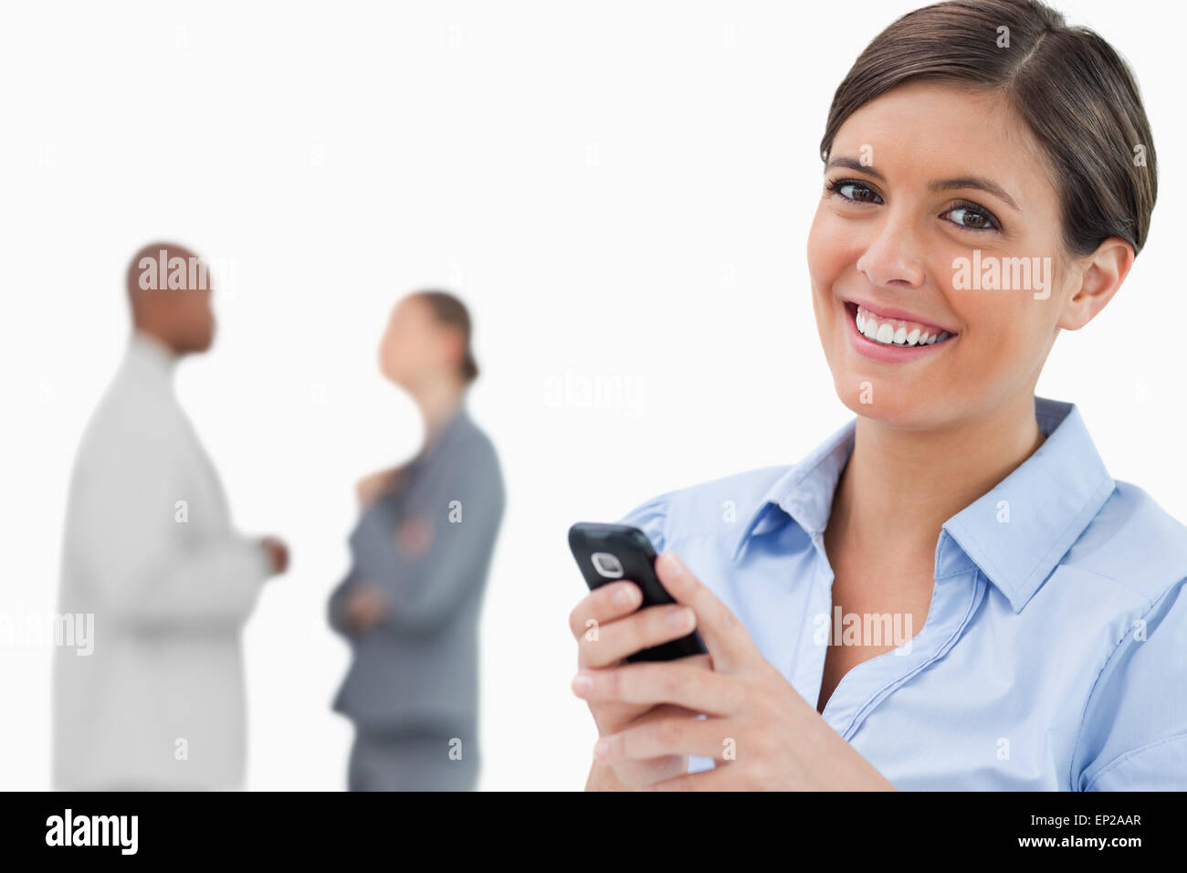 Smiling saleswoman with mobile phone and associates behind her Stock ...