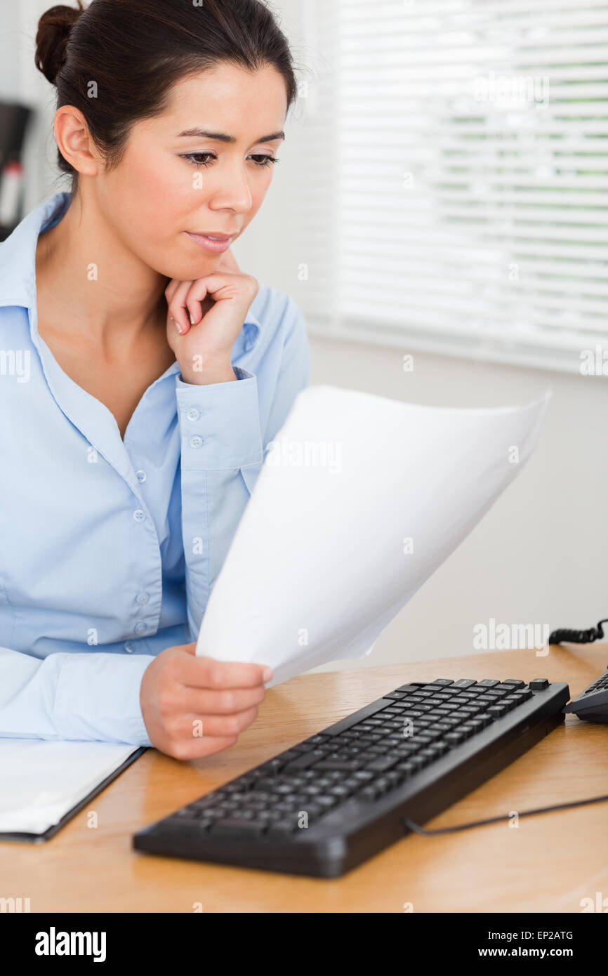 Attractive woman looking at a computer screen while holding a sheet of ...