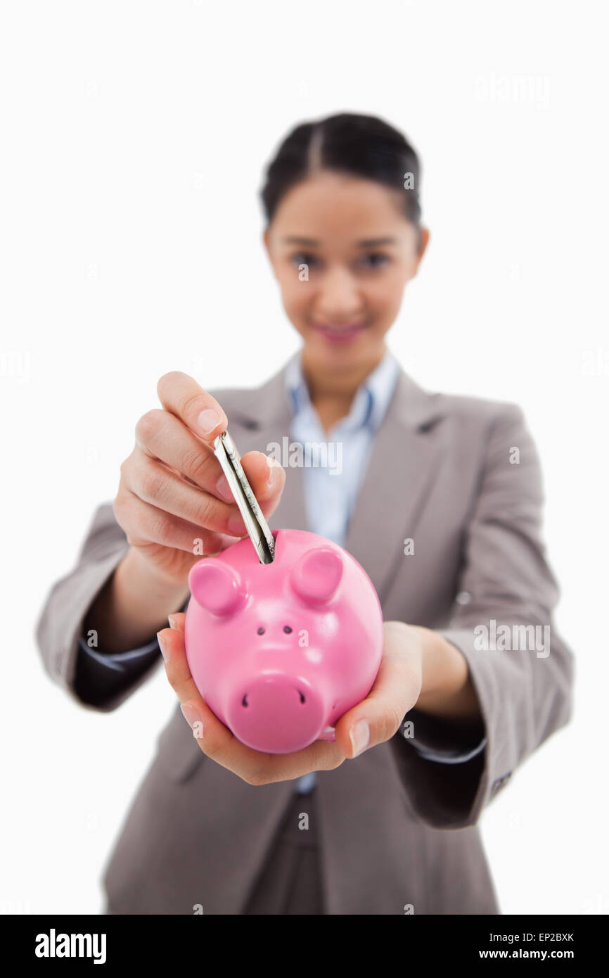 Portrait of a young businesswoman putting a bank note in a piggy bank ...