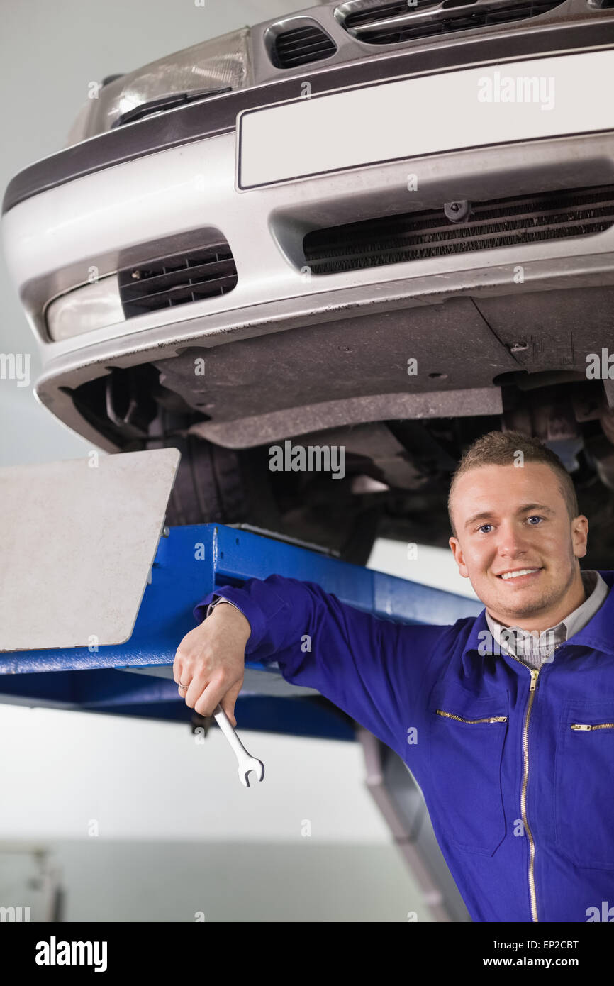 Smiling mechanic holding a spanner below a car Stock Photo - Alamy