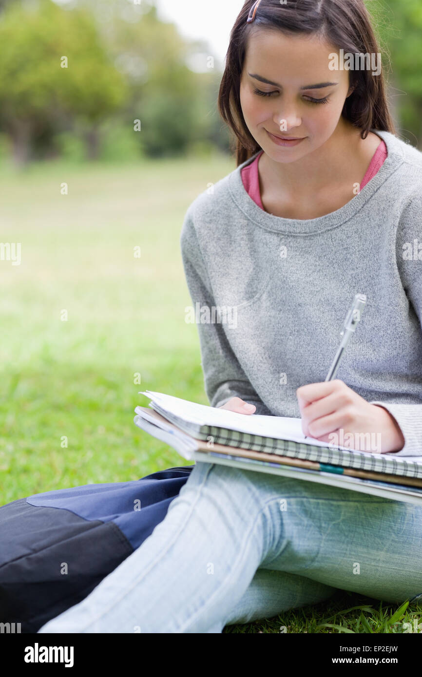 Young smiling girl writing on her notebook while sitting in a park ...
