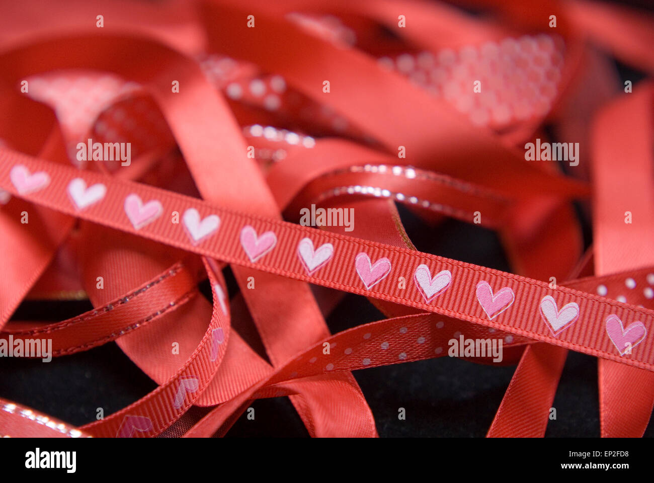 A tangle of red ribbons with love hearts scattered on a black ...