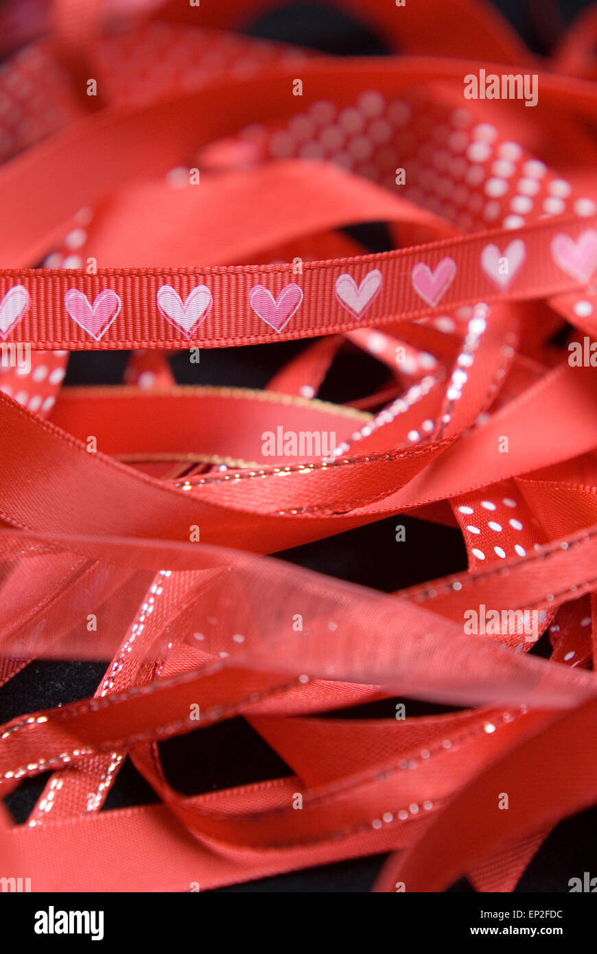 A tangle of red ribbons with love hearts scattered on a black ...