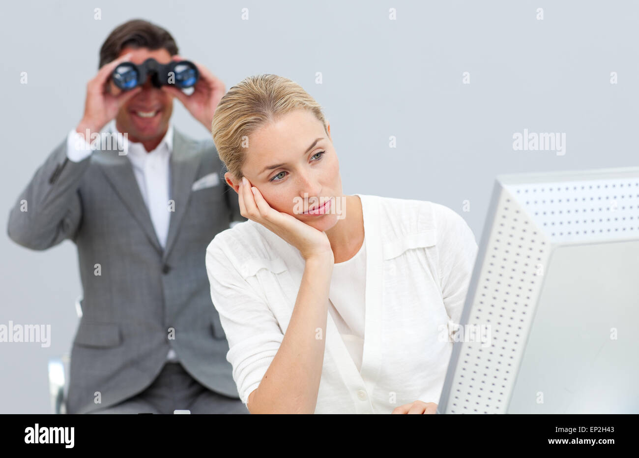 Smiling manager holding binoculars looking at his colleague's computer ...