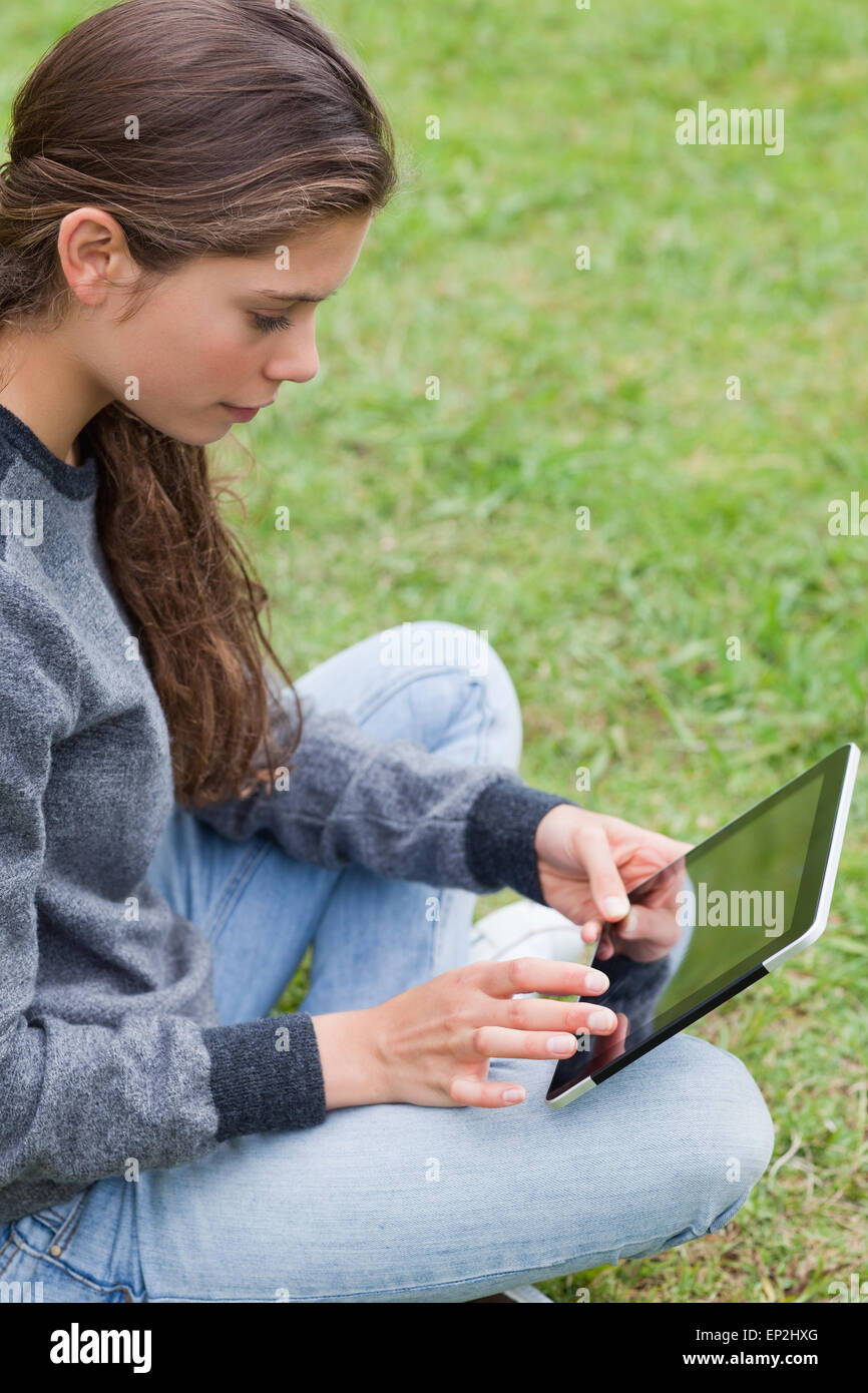 Young smiling girl sitting cross-legged while touching her tablet pc ...