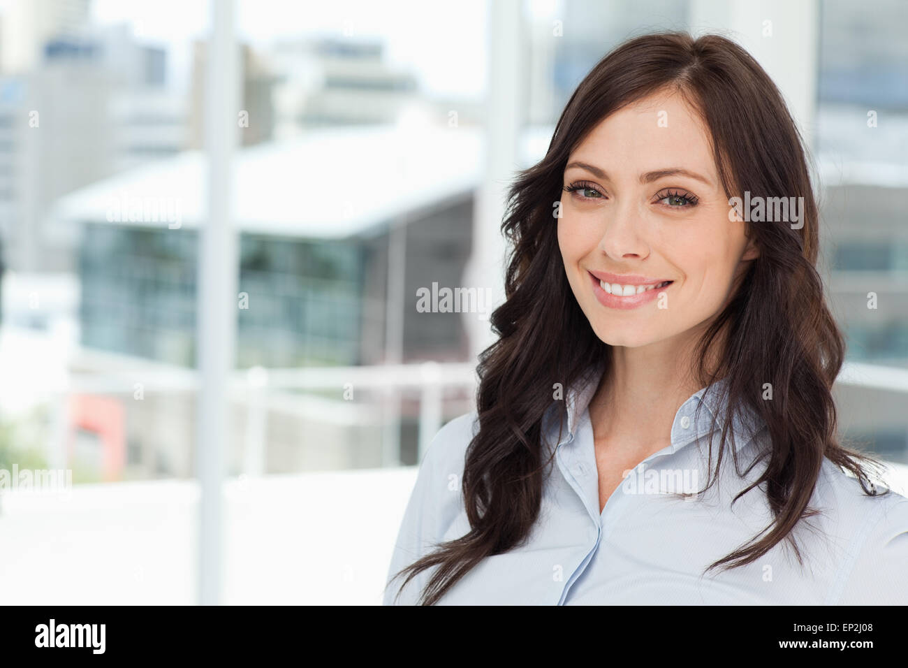 Young smiling executive woman standing upright in front of the window ...