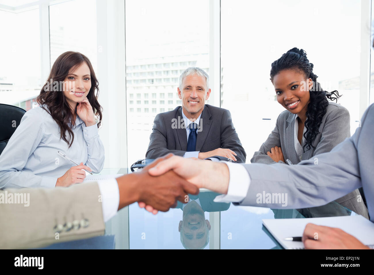 Three smiling co-workers looking at two business people shaking hands ...
