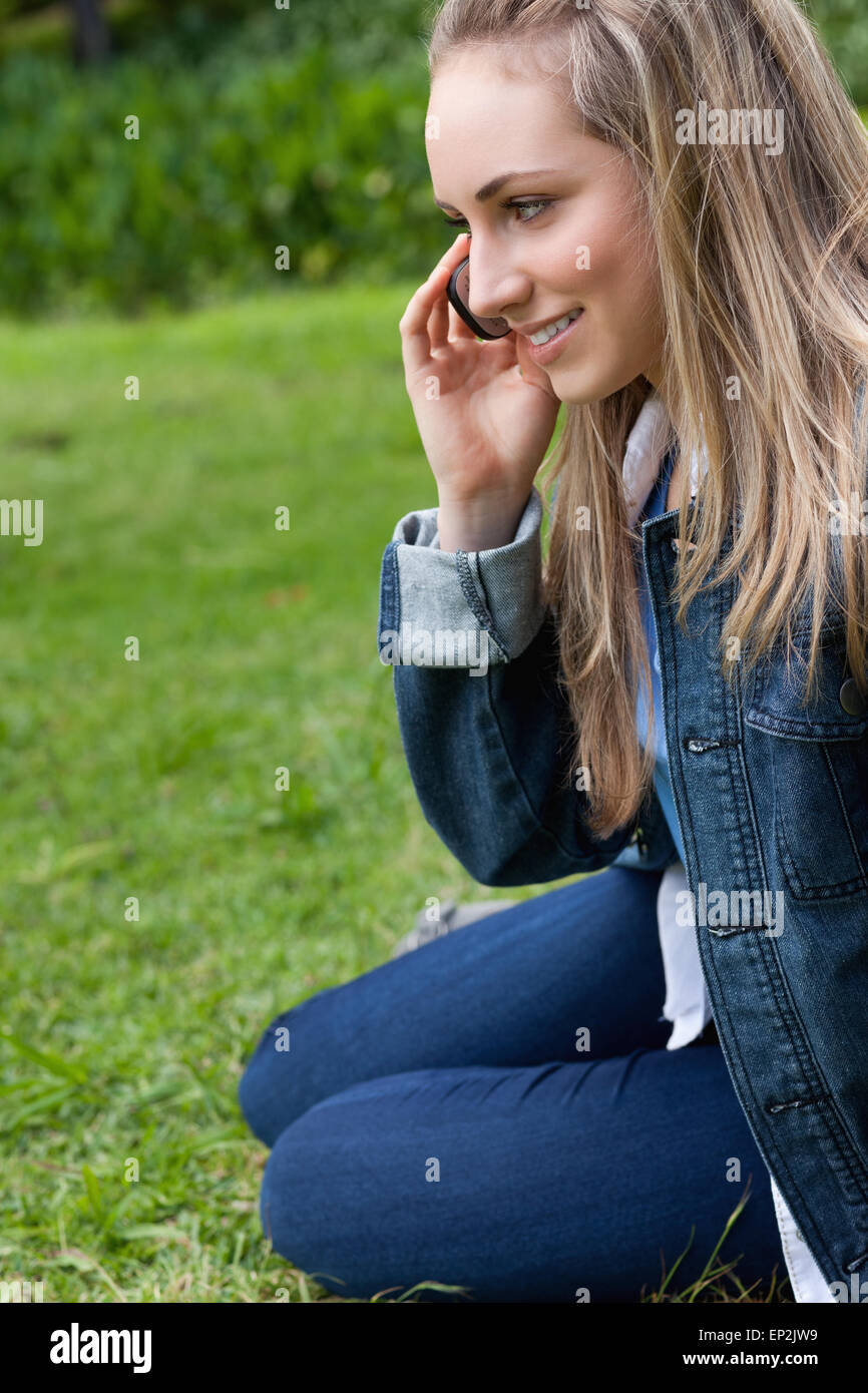 Young smiling girl talking on the phone while sitting on the grass ...
