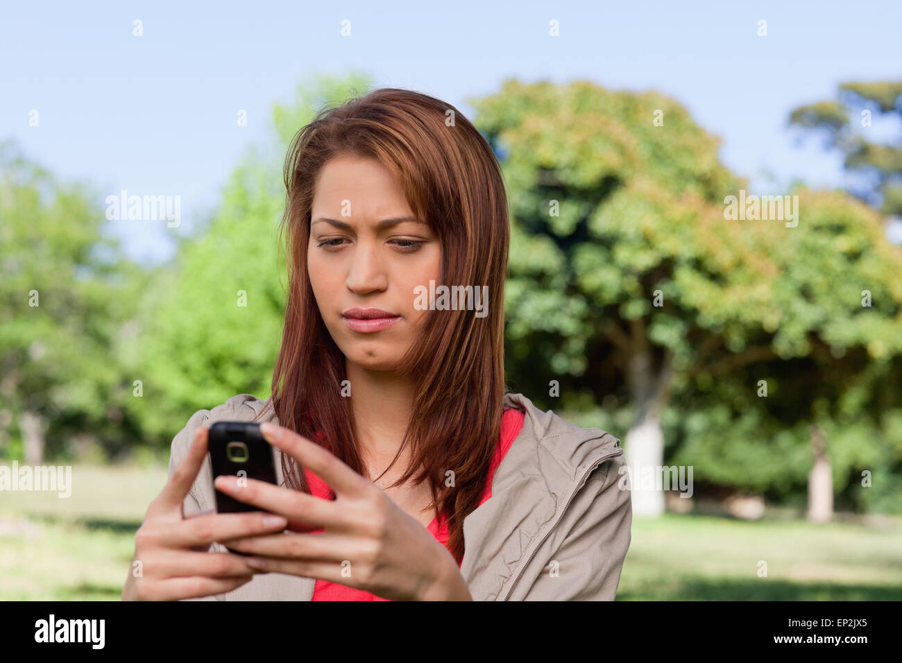 Serious woman reading a text message in a bright grassland area Stock ...
