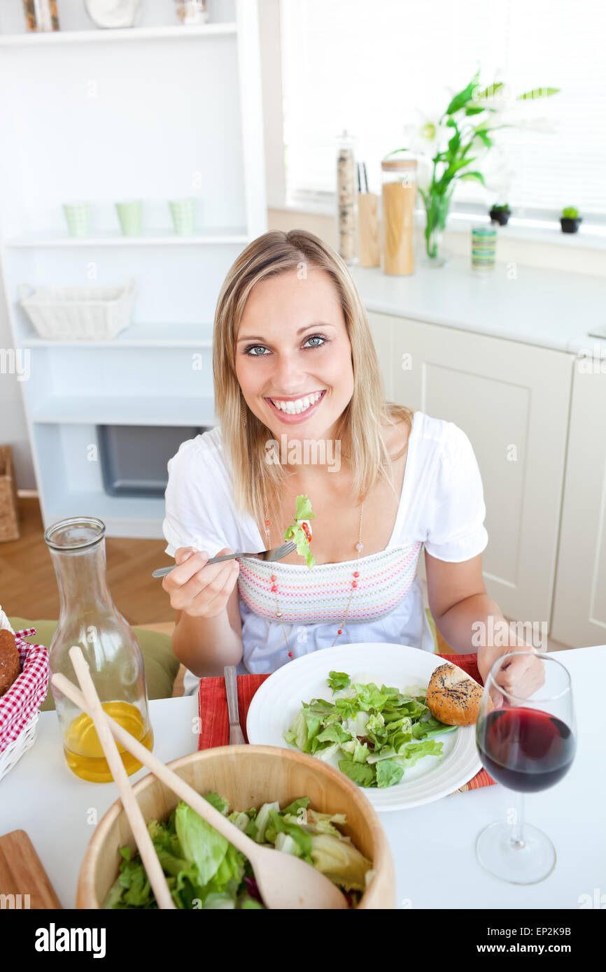 Smiling woman eating salad in the kitchen Stock Photo - Alamy