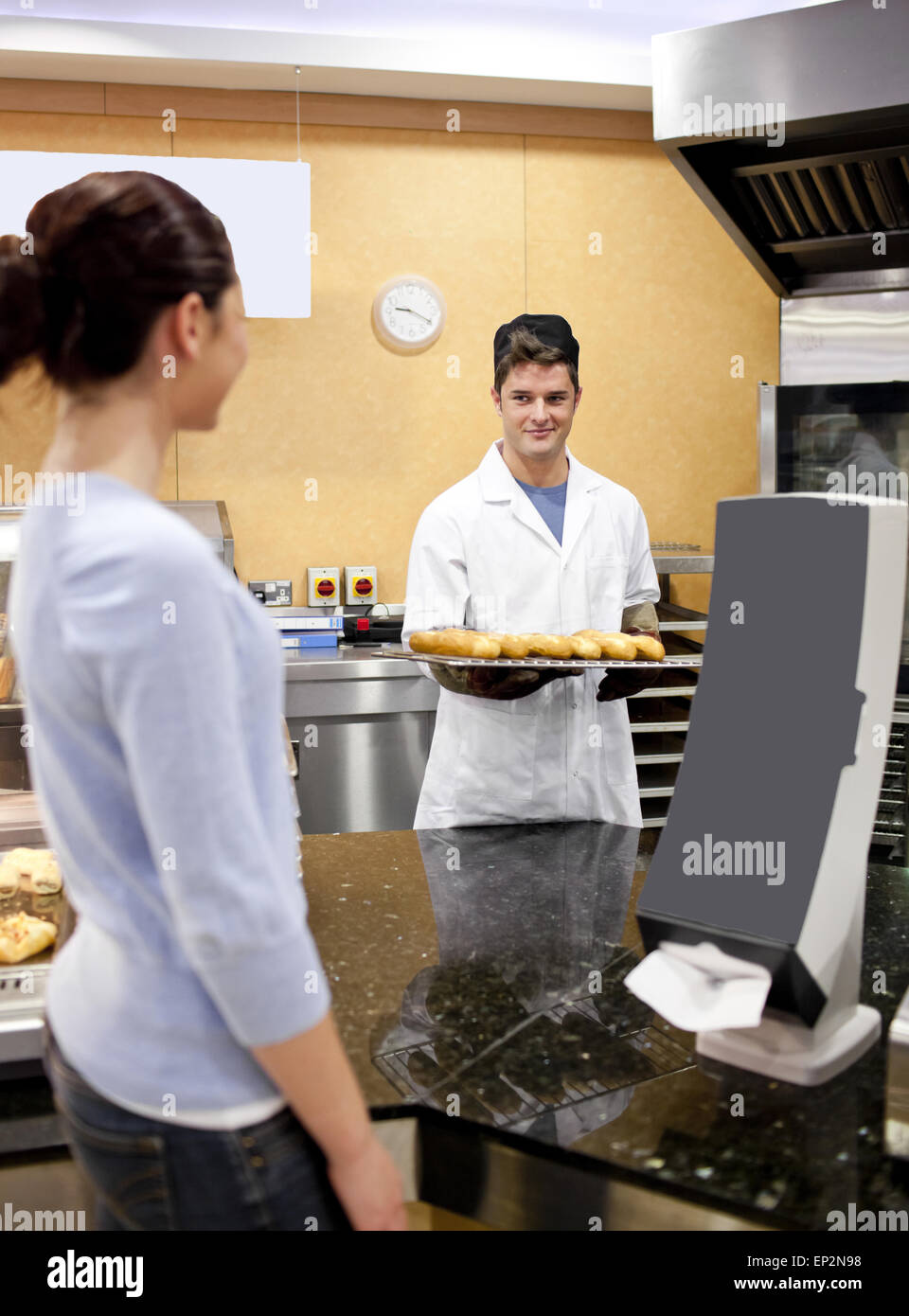 Portrait of a baker holding bread and baguette smiling at a customer in ...