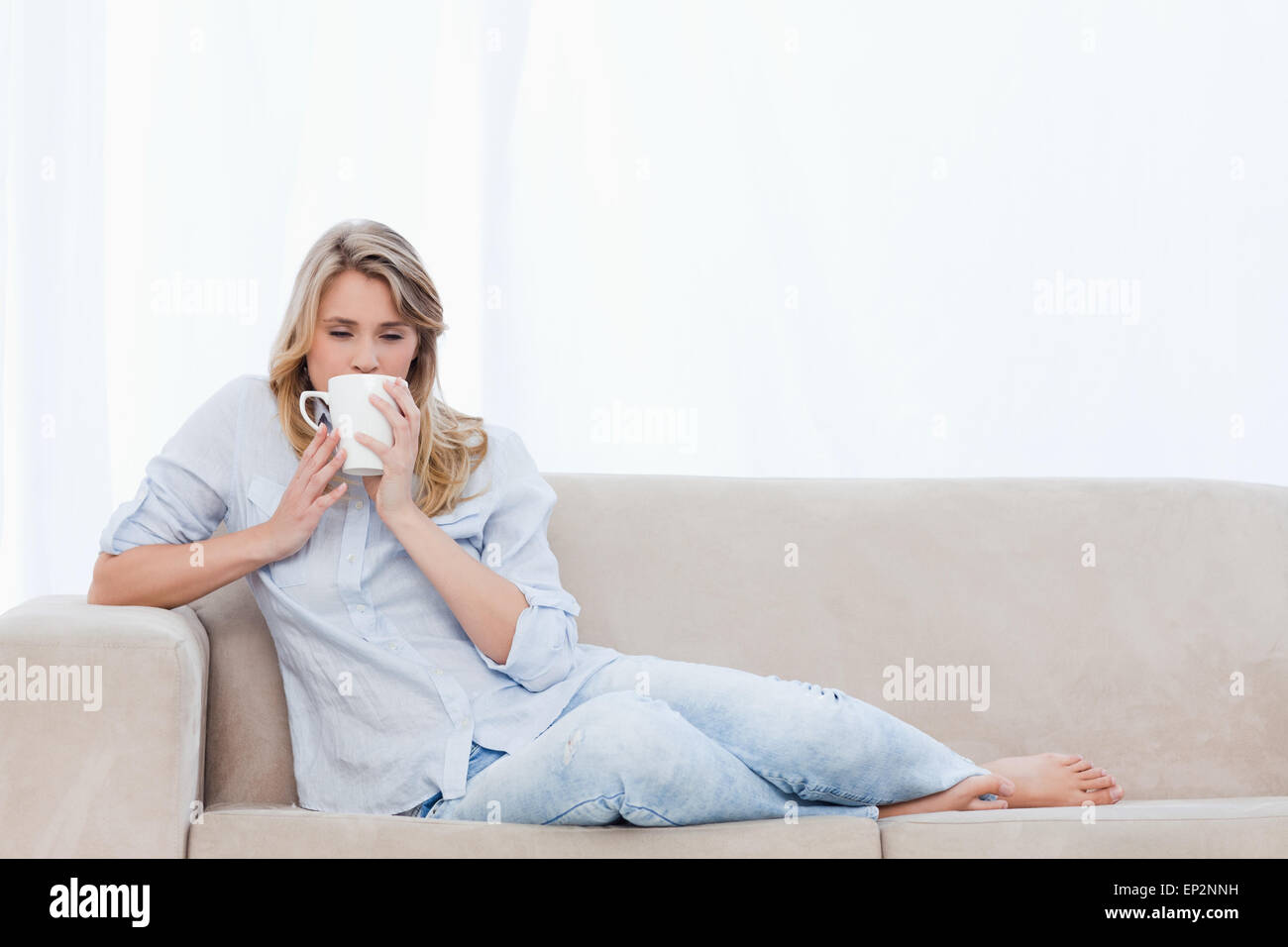 A woman drinking a cup of coffee is lying on a couch Stock Photo - Alamy