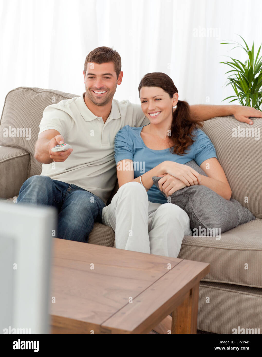 Happy man changing channel while watching television with his wife ...