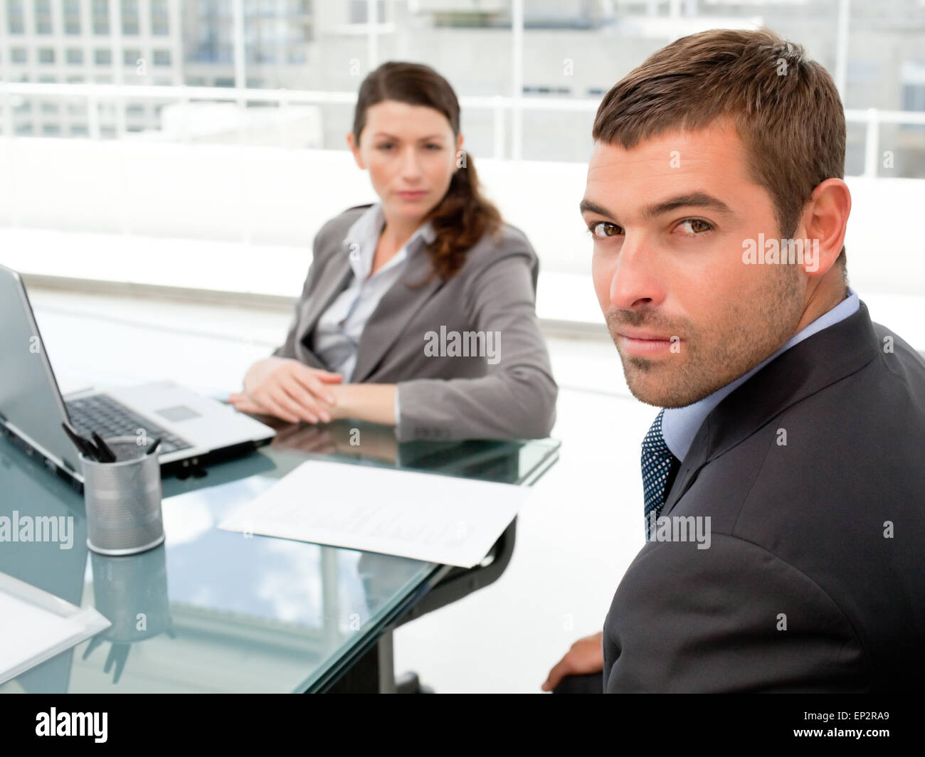 Serious businesspeople sitting around a table and looking at the camera ...