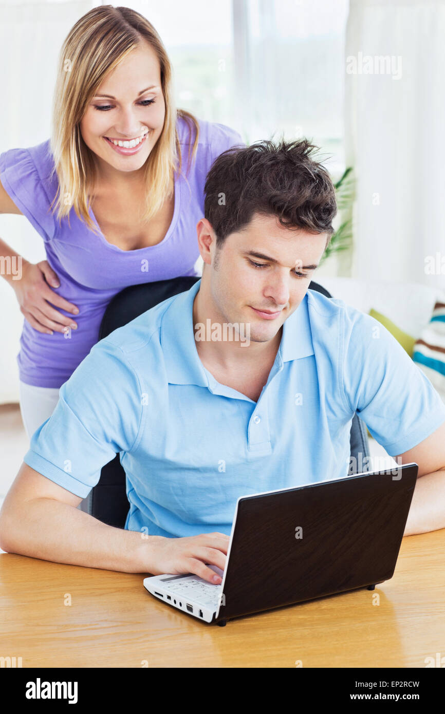 Serious man using his laptop with his girlfriend behind him watching ...