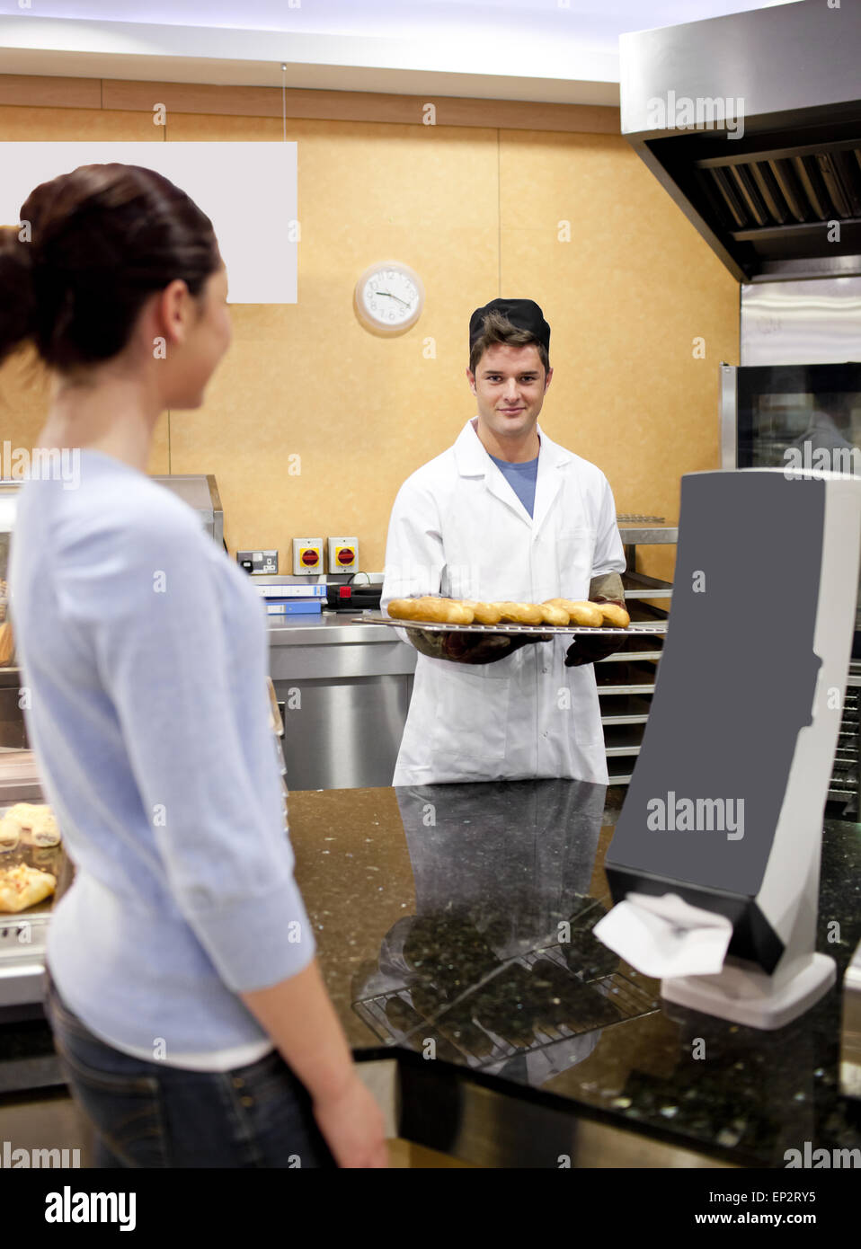 Young baker holding bread and baguette smiling at a customer in the ...