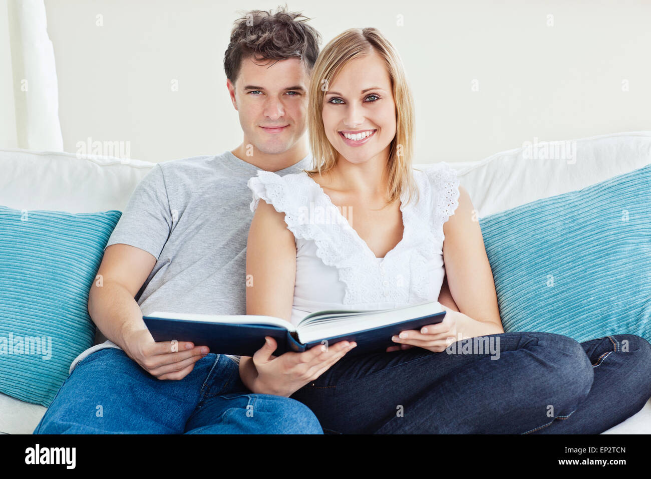 Cute couple reading a book together sitting on the couch at home Stock ...