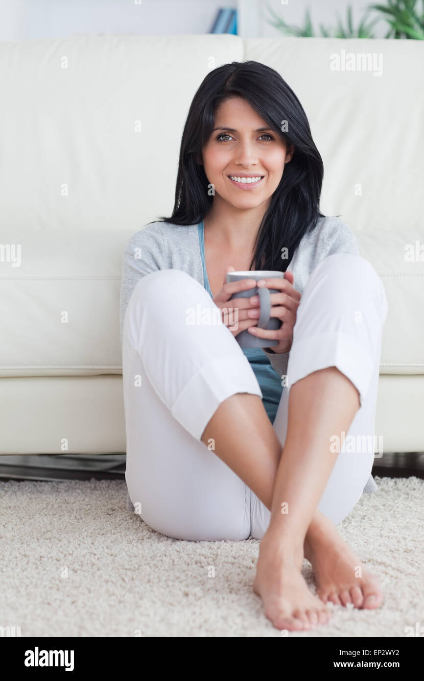 Woman holding a mug with two hands and crossing her legs while sitting ...