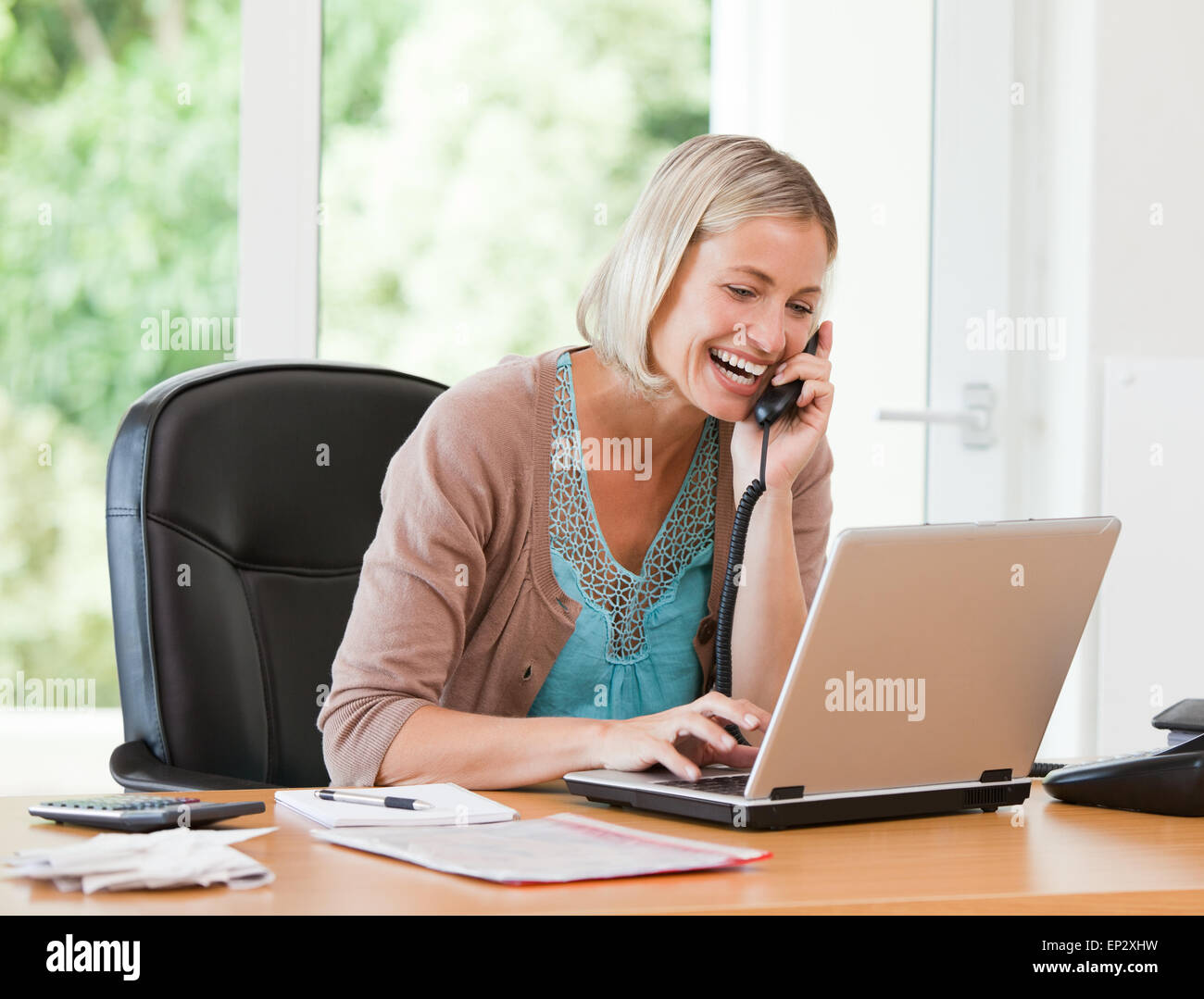 Woman working on her computer while she is phoning Stock Photo - Alamy