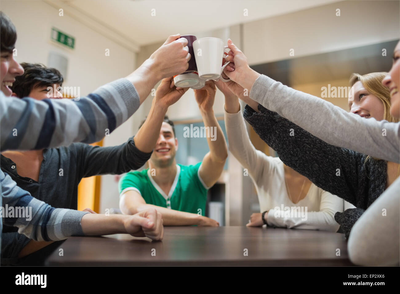 Students sitting around the table clinking mugs Stock Photo - Alamy