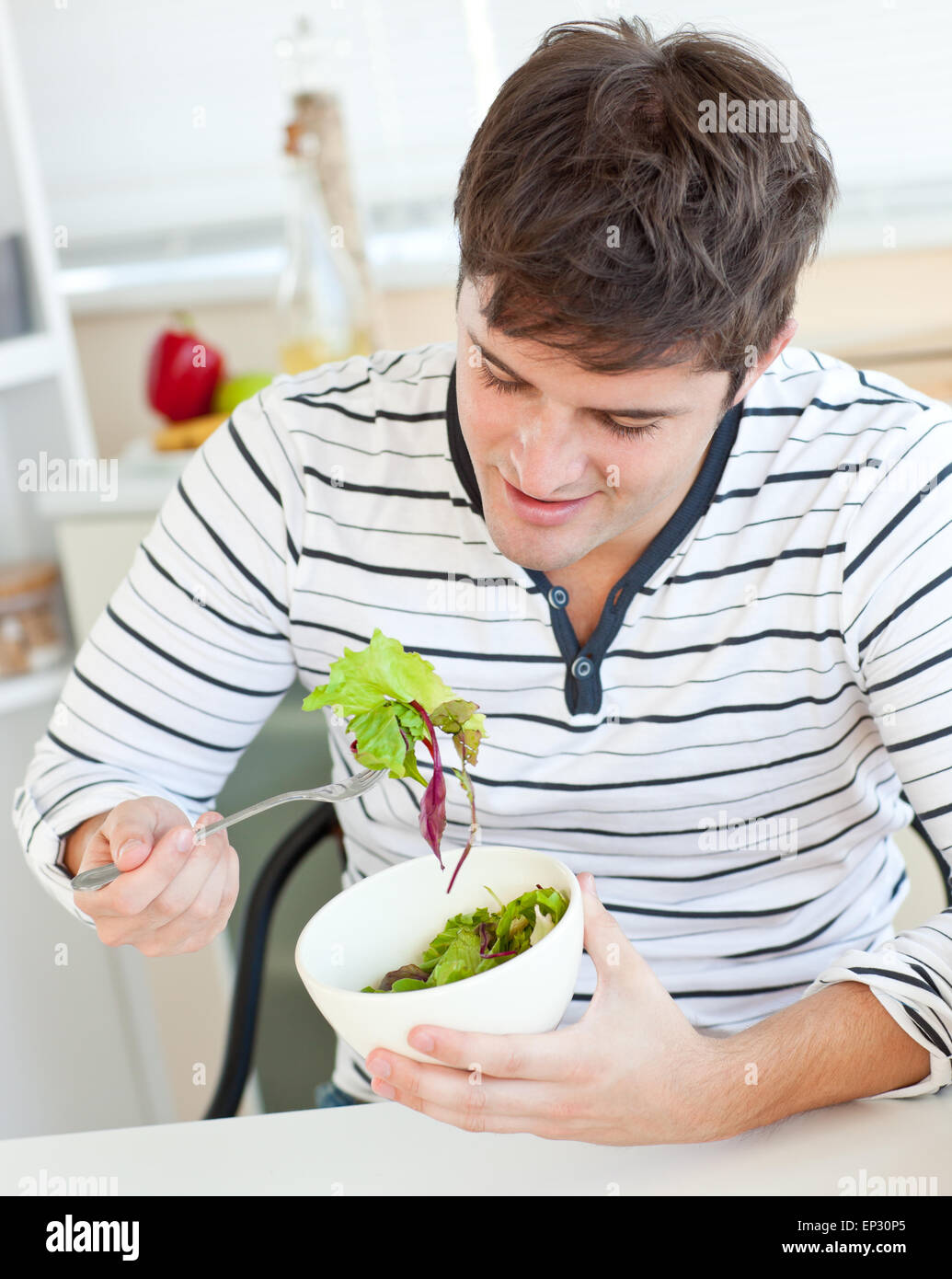 Delighted young man eating a healthy salad in the kitchen Stock Photo ...