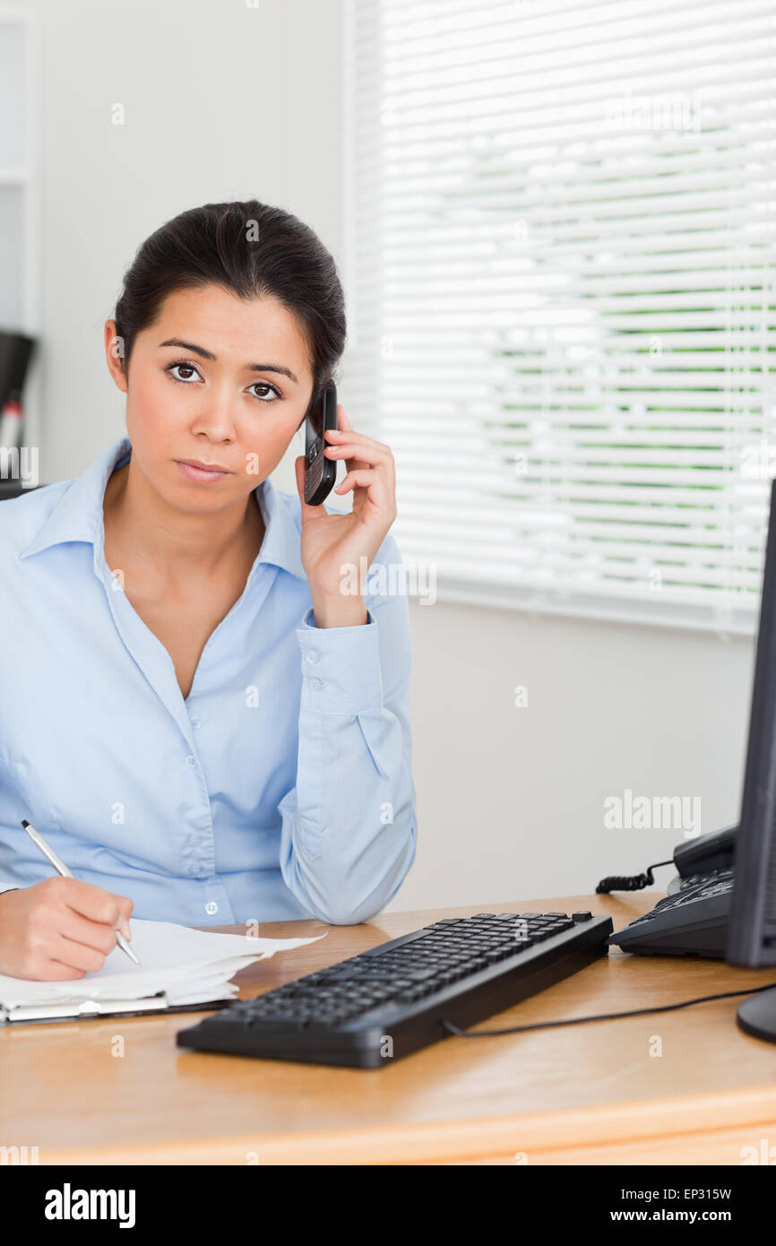 Beautiful woman using her mobile phone while writing on a sheet of ...