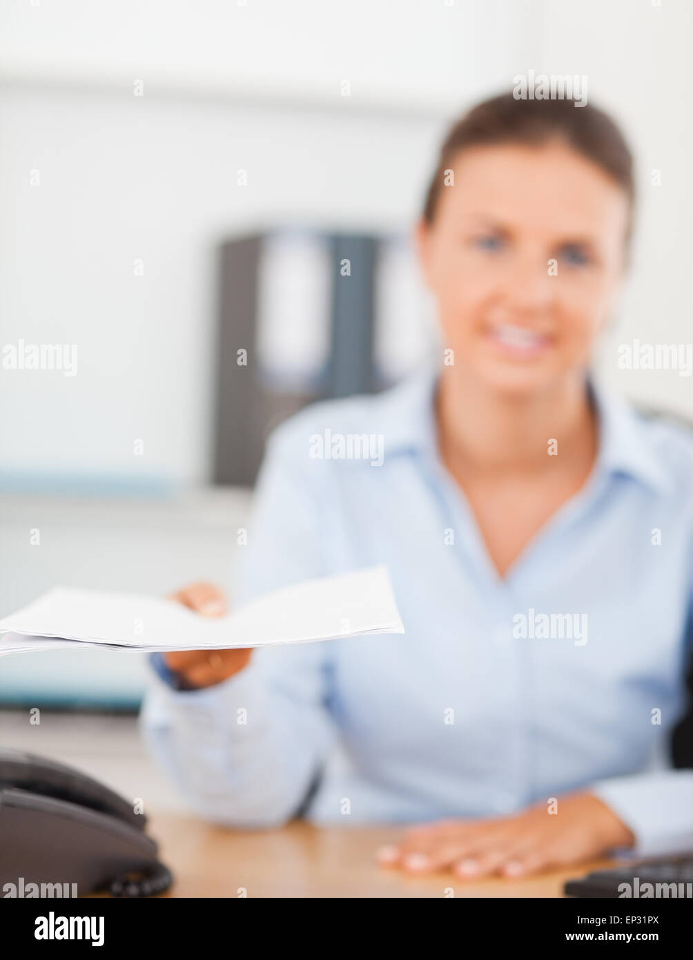 Smiling brunette businesswoman handing out a paper Stock Photo - Alamy