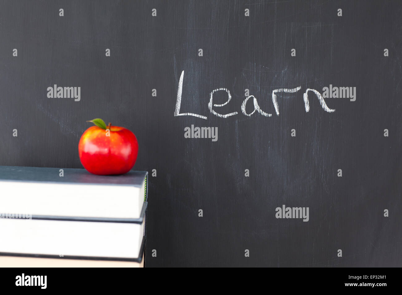 Stack of books with a red apple and a blackboard with learn written on ...