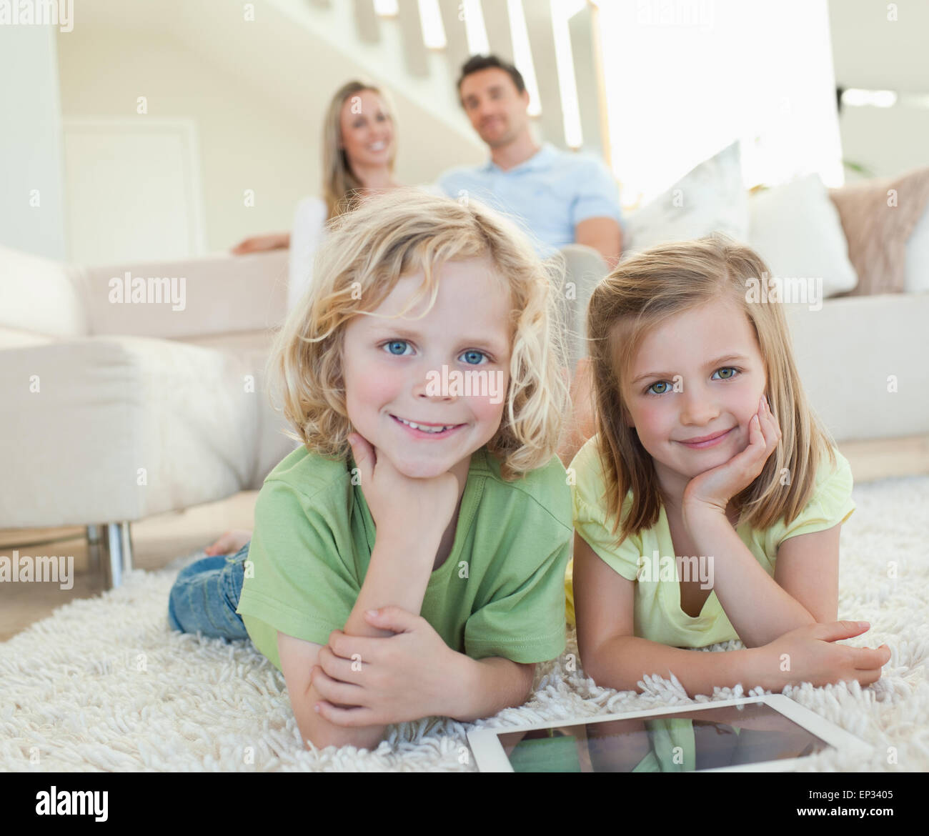 Children on the carpet with tablet and parents behind them Stock Photo ...
