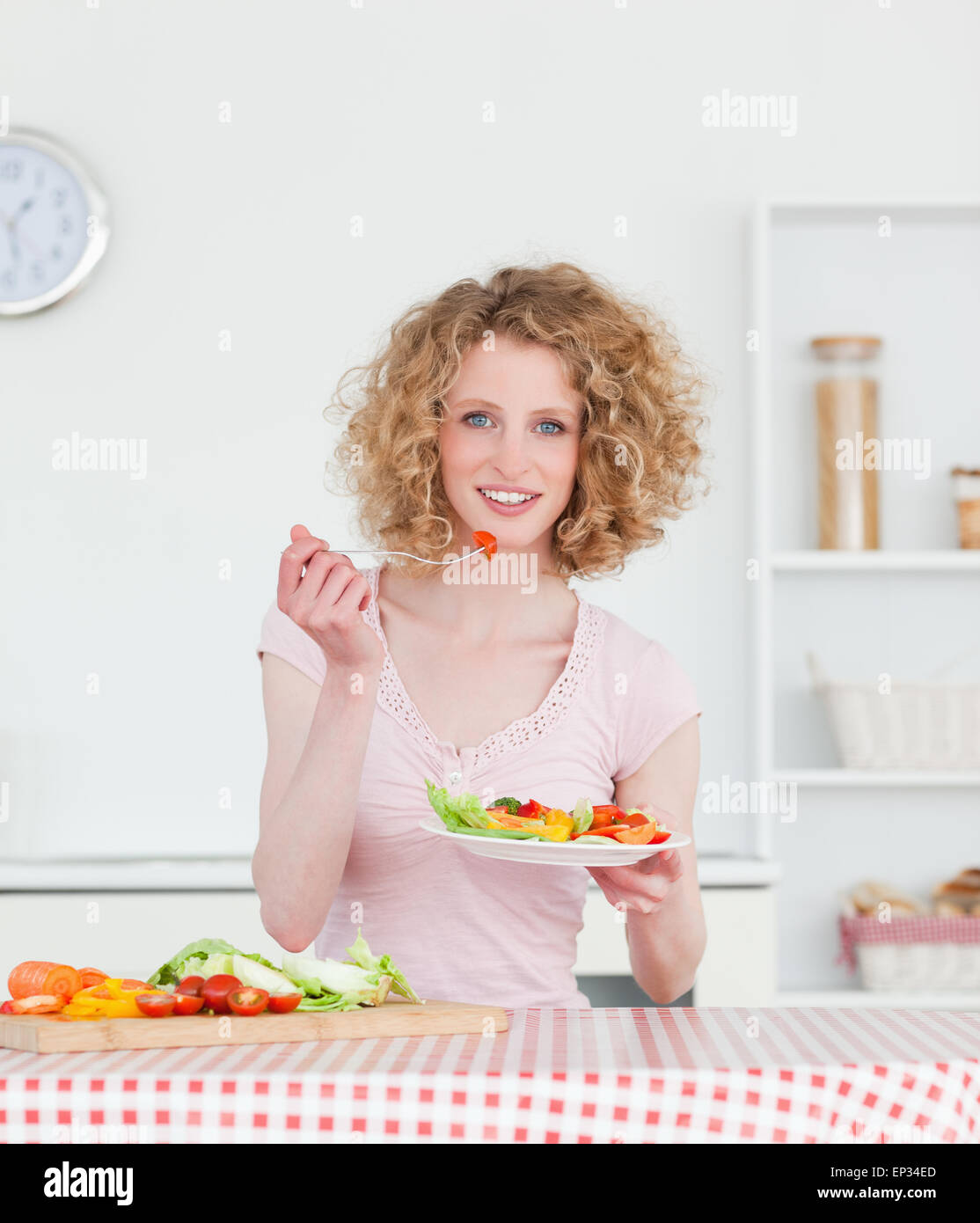 Pretty blonde woman eating some vegetables in the kitchen Stock Photo ...