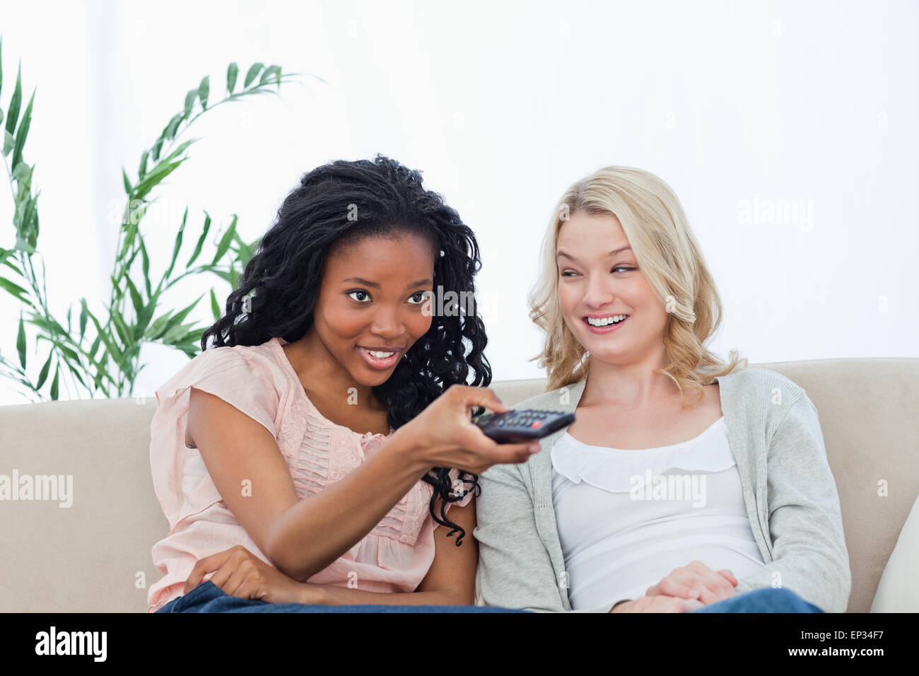 A woman is smiling at her friend who is holding a television remote ...
