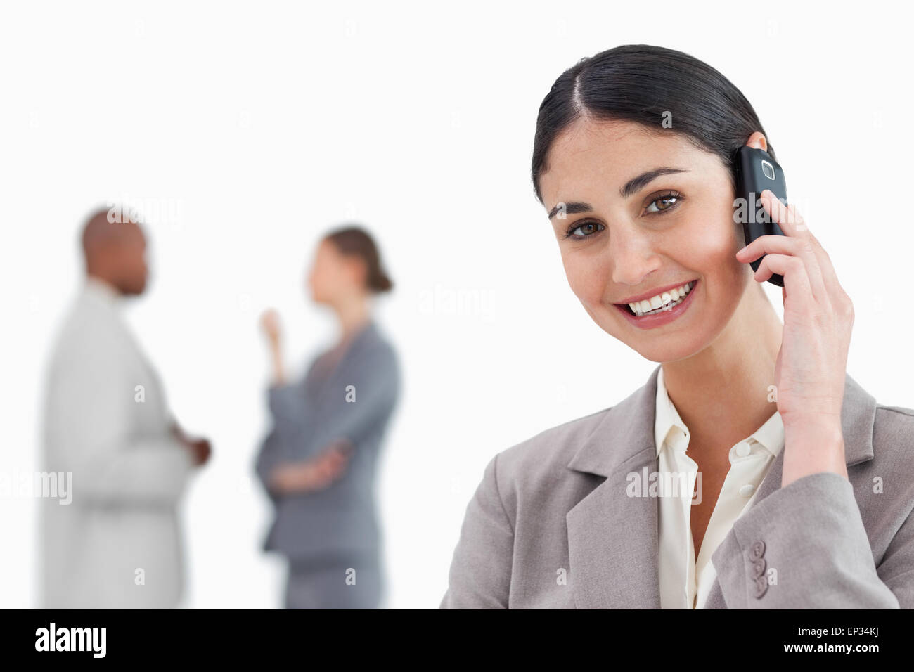 Smiling saleswoman with mobile phone and colleagues behind her Stock ...
