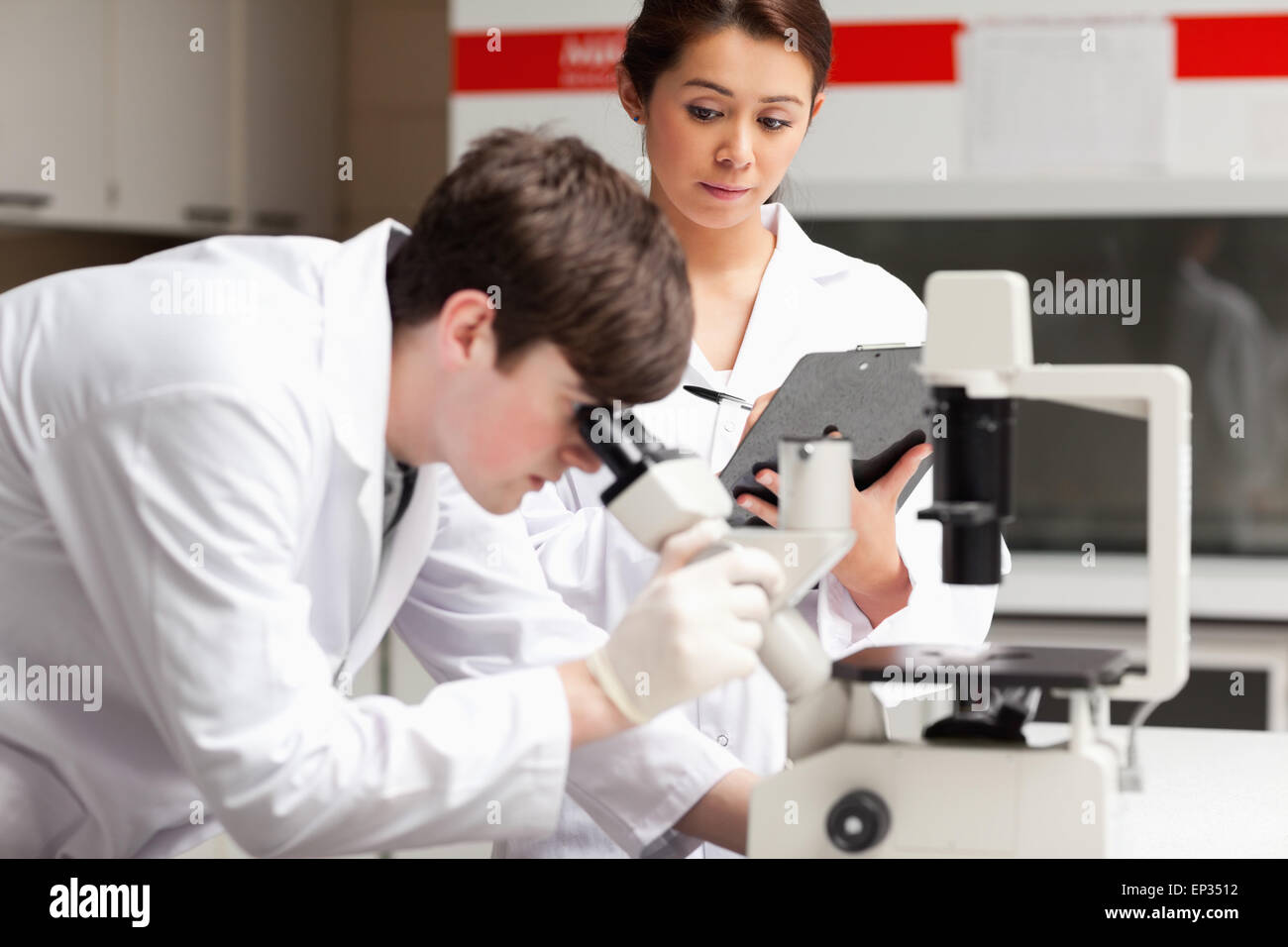 Science student looking in a microscope while his classmate is w Stock ...