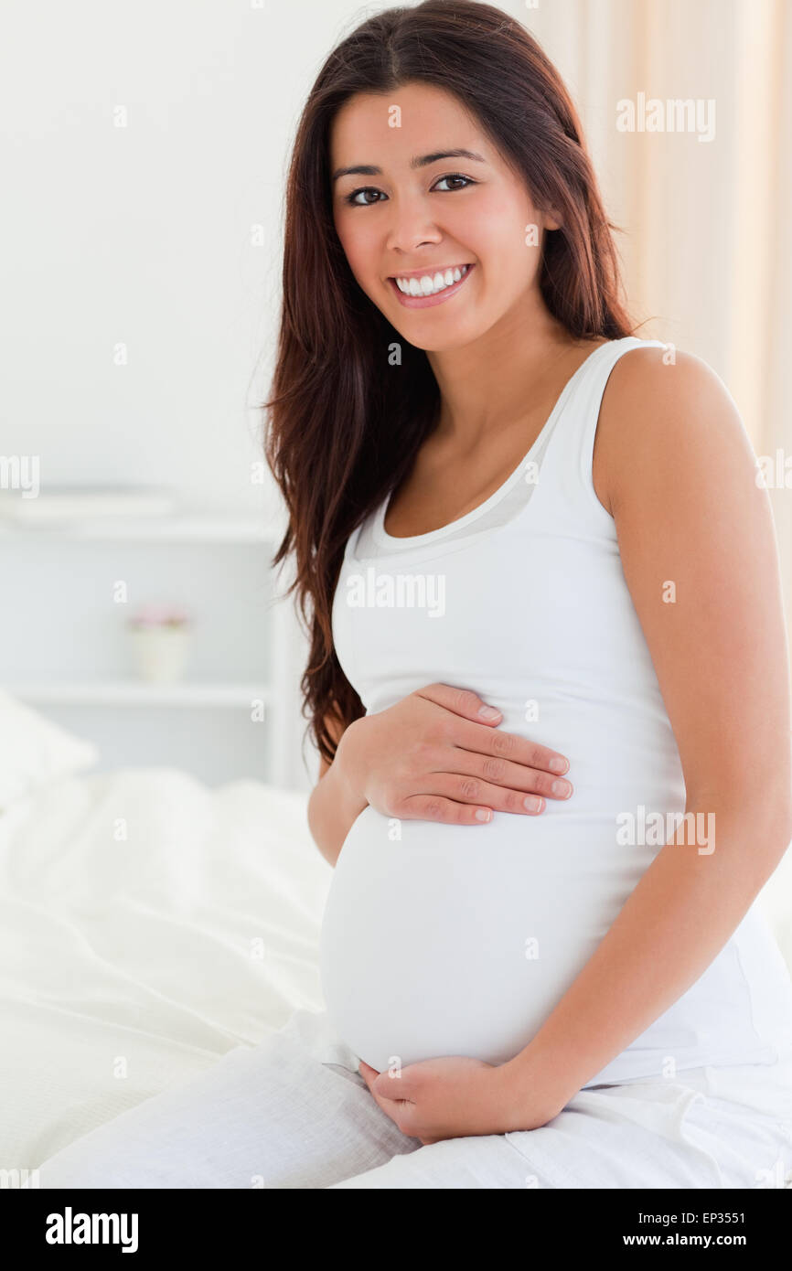 Portrait of a good looking pregnant woman touching her belly while ...