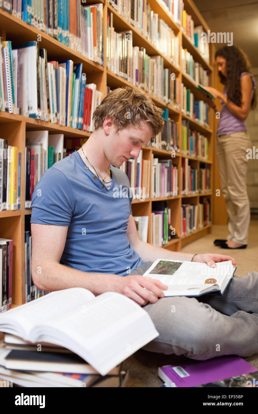 Portrait of a male student reading books while his classmate is Stock ...