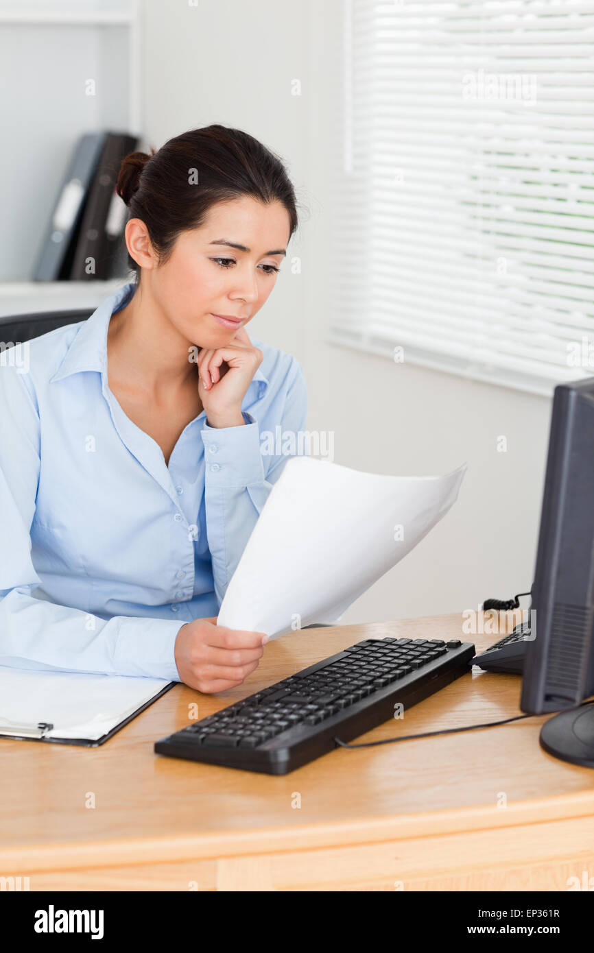 Beautiful woman looking at a computer screen while holding a sheet of ...