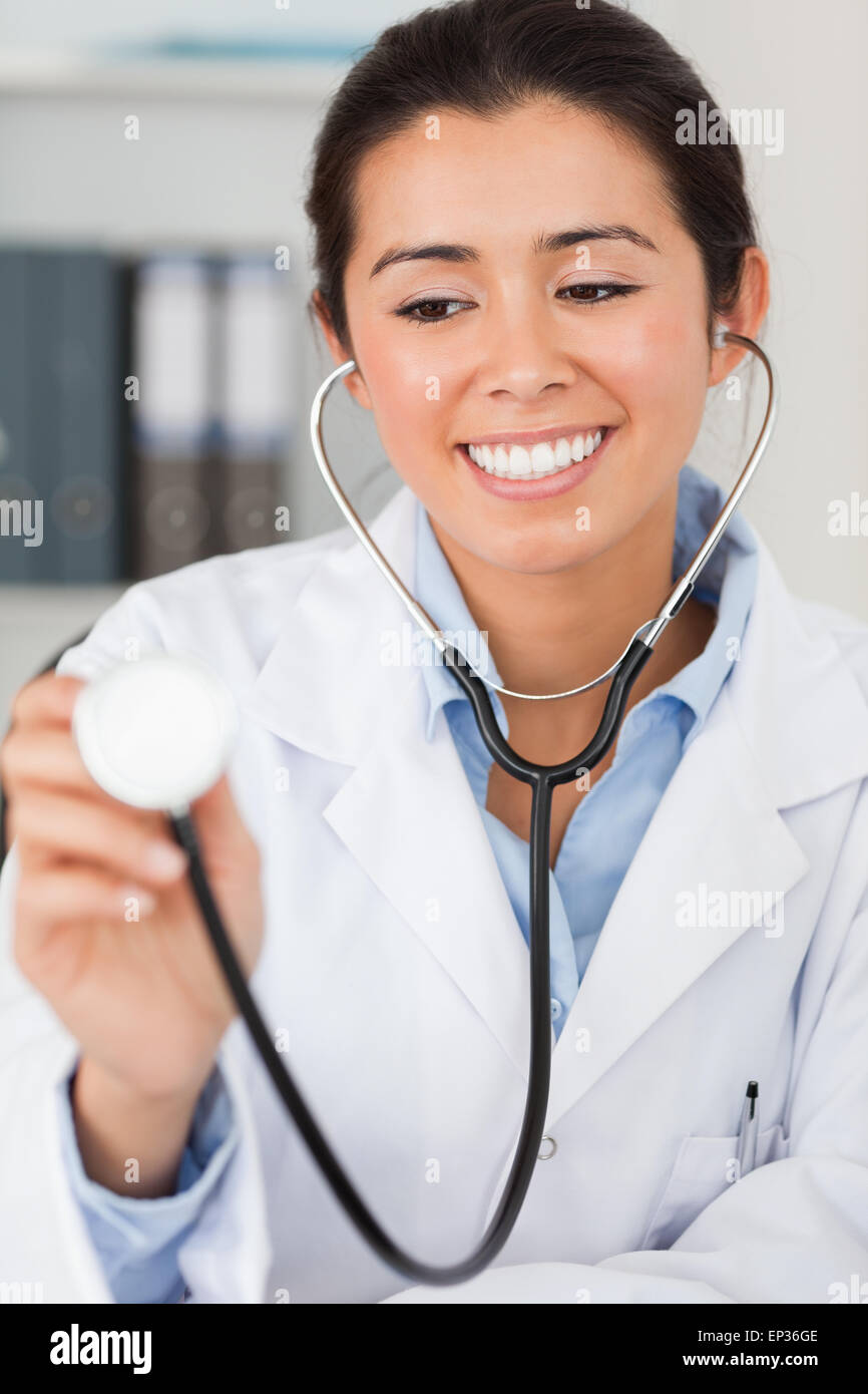 Pretty female doctor using a stethoscope while looking at the camera ...