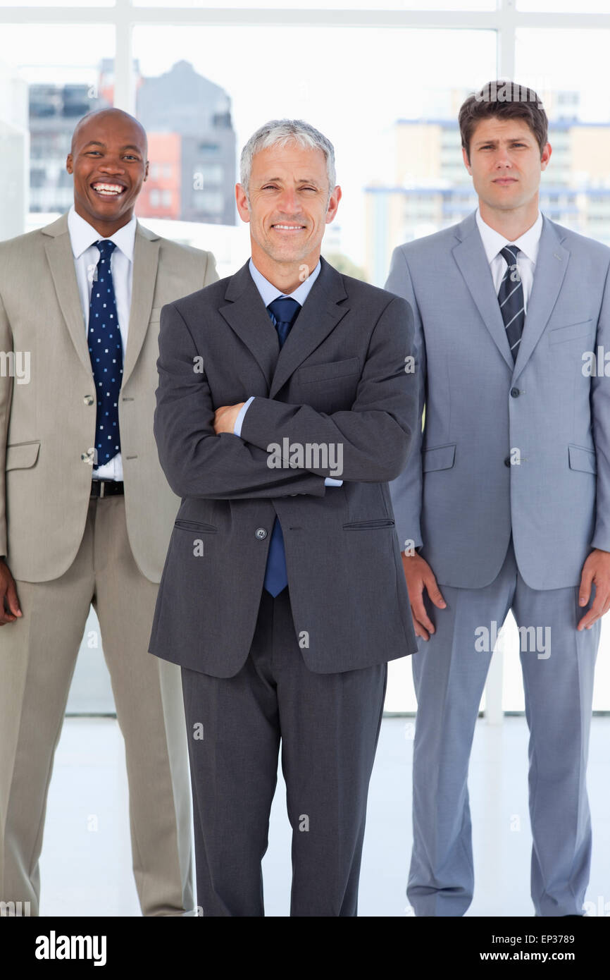 Mature director standing in front of a relaxed co-worker and a serious ...
