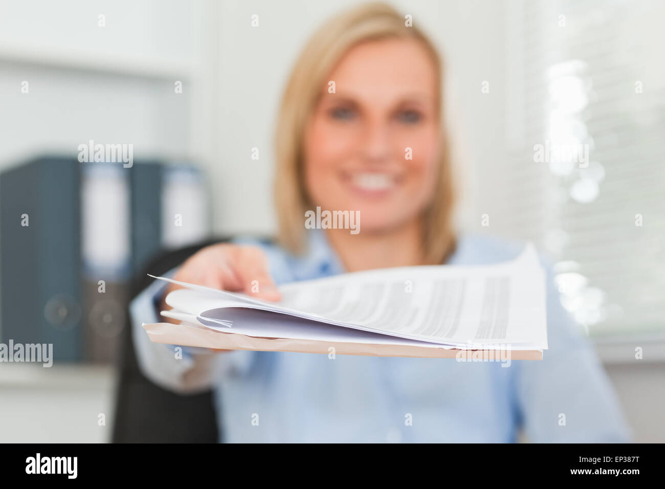 Smiling businesswoman passing a paper looks into camera Stock Photo - Alamy
