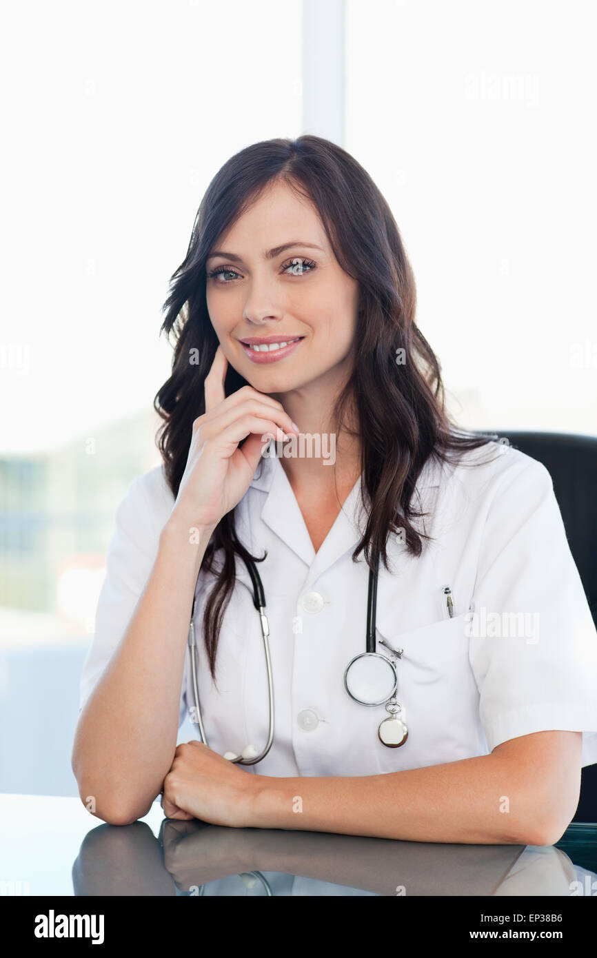 Smiling doctor sitting at the desk with her finger on her cheek Stock ...