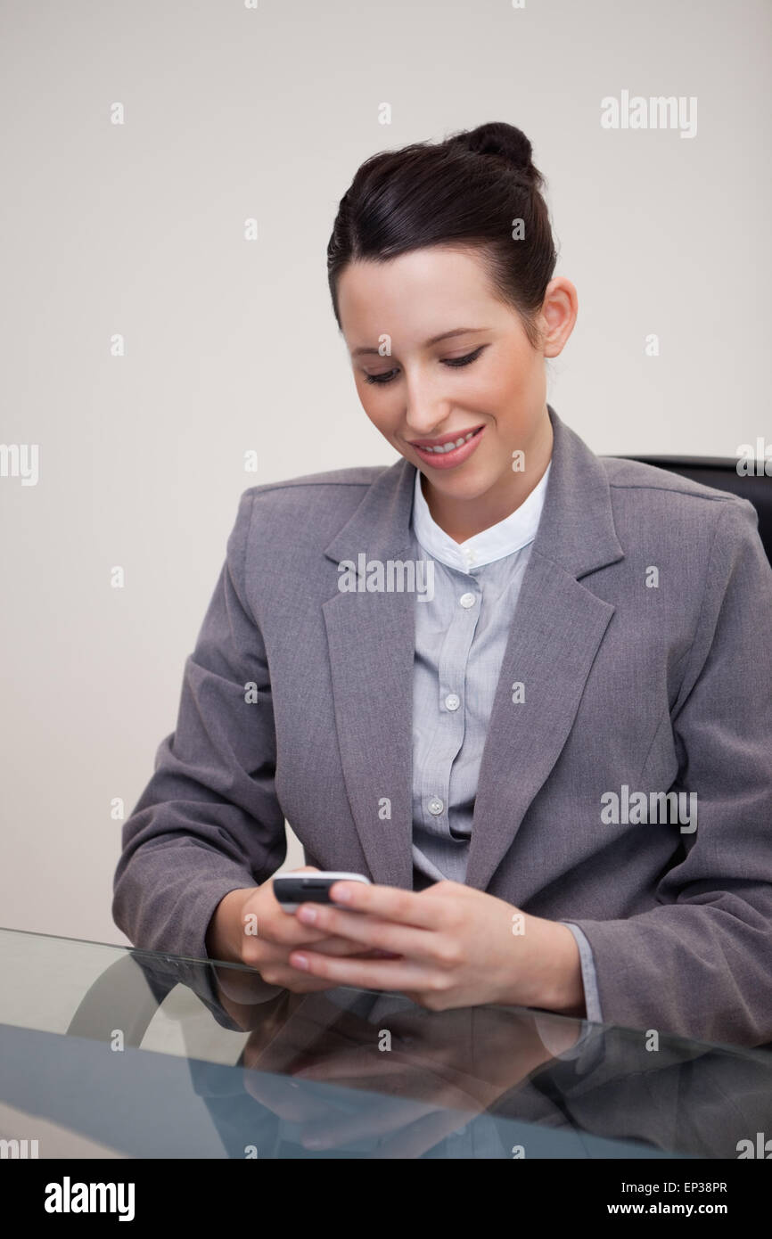 Smiling businesswoman sitting behind desk writing a textmessage Stock ...