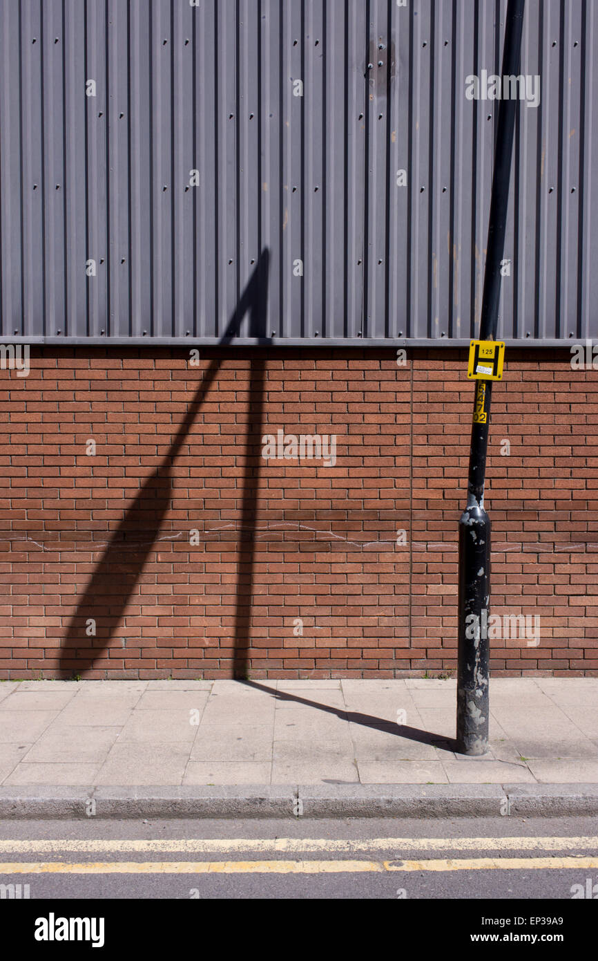 Leaning post and its own shadow on a brick wall in south London. In an ...