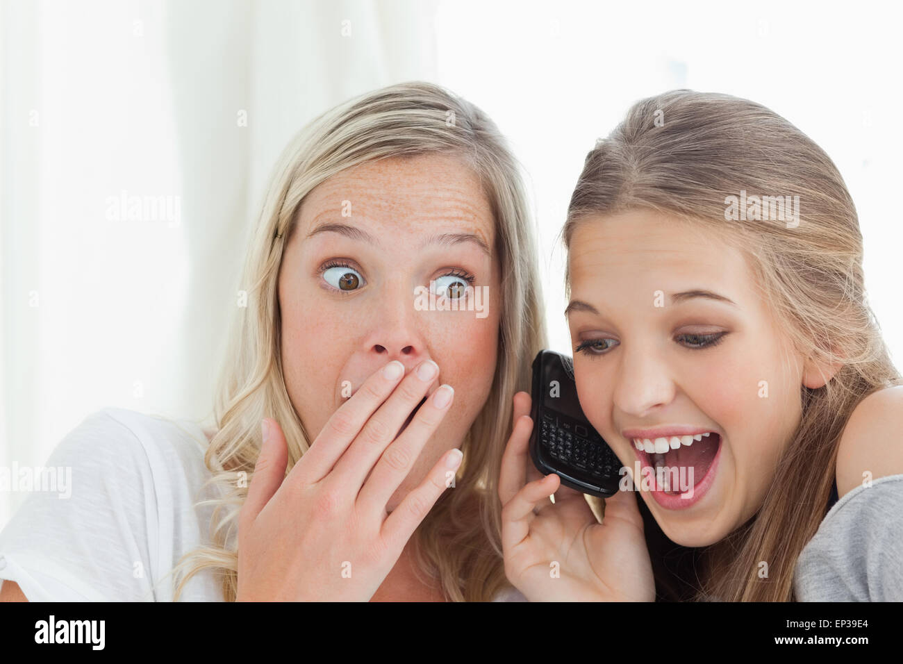Shocked and happy sisters listening to a phone call Stock Photo - Alamy