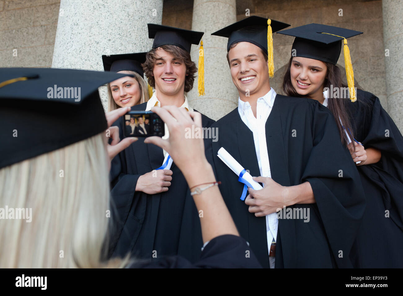 Close-up of a blonde graduate taking a picture of her friend Stock ...