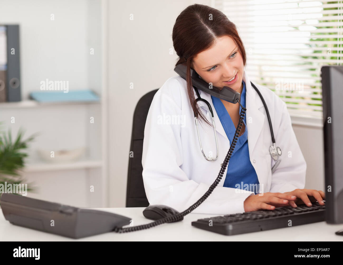 Female doctor telephoning whilst typing Stock Photo - Alamy