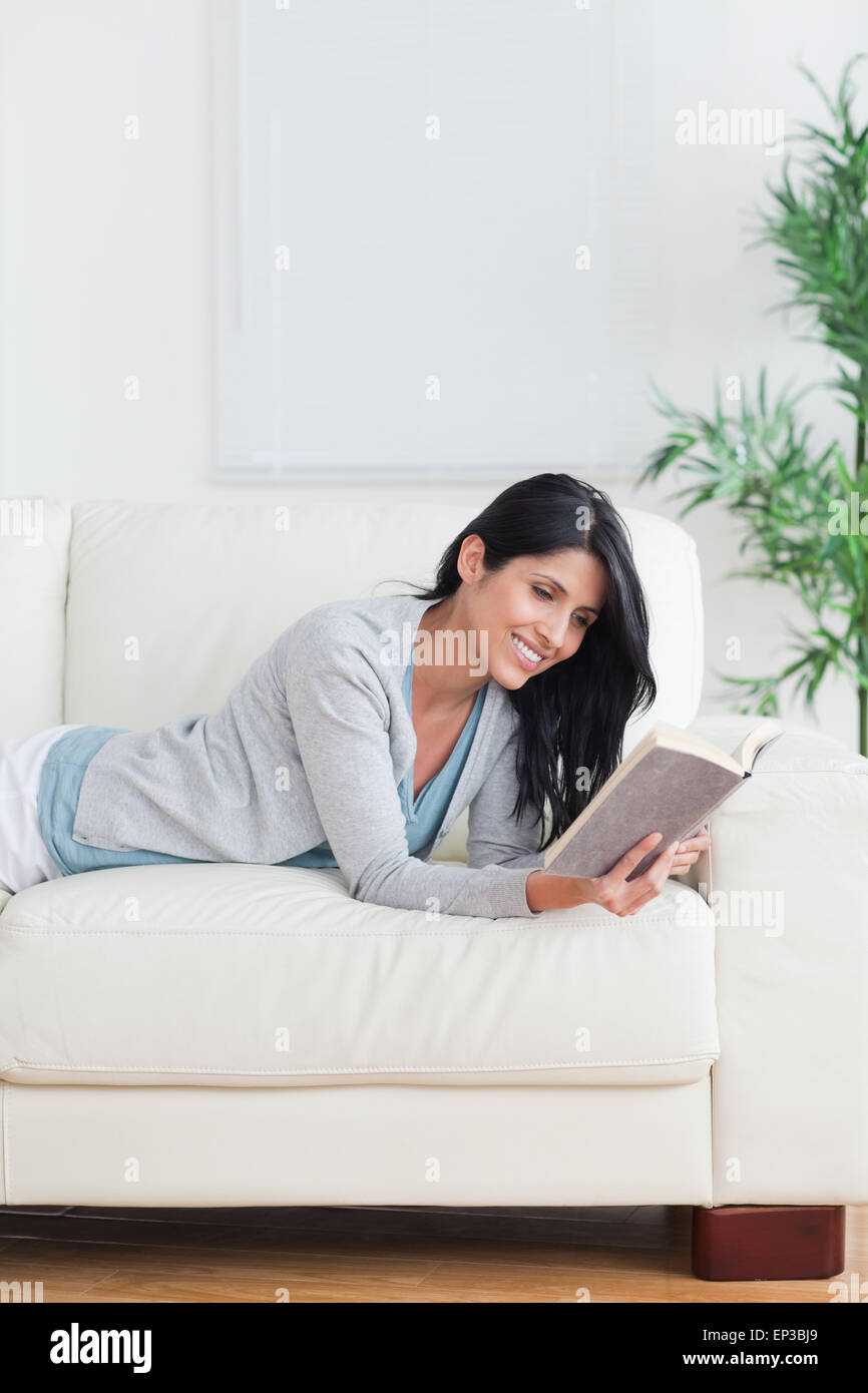Smiling woman reading a book while she lays on a couch Stock Photo - Alamy
