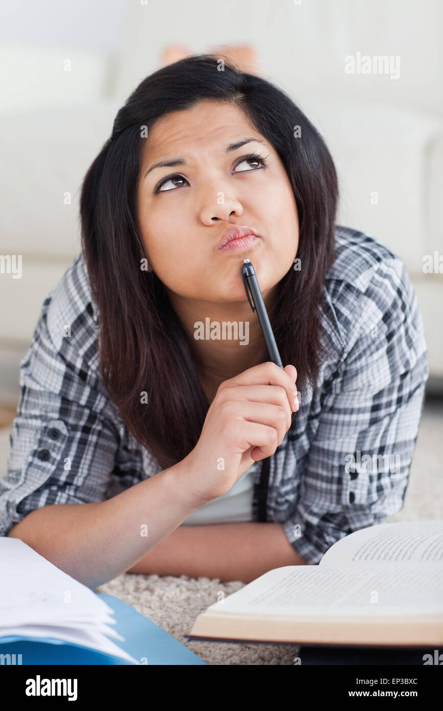 Thinking woman laying on the floor while holding a pen with a book ...