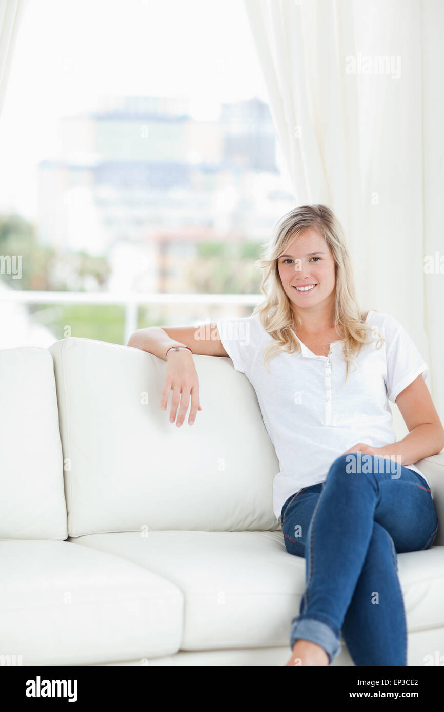 A woman with her arm resting on the couch as she sits and smiles Stock ...
