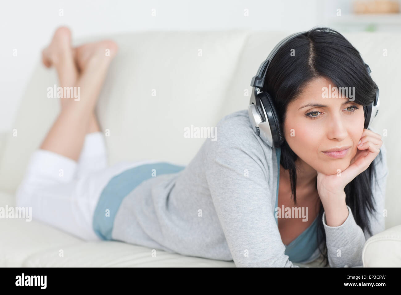 Woman thinking with headphones on while laying on a couch Stock Photo ...