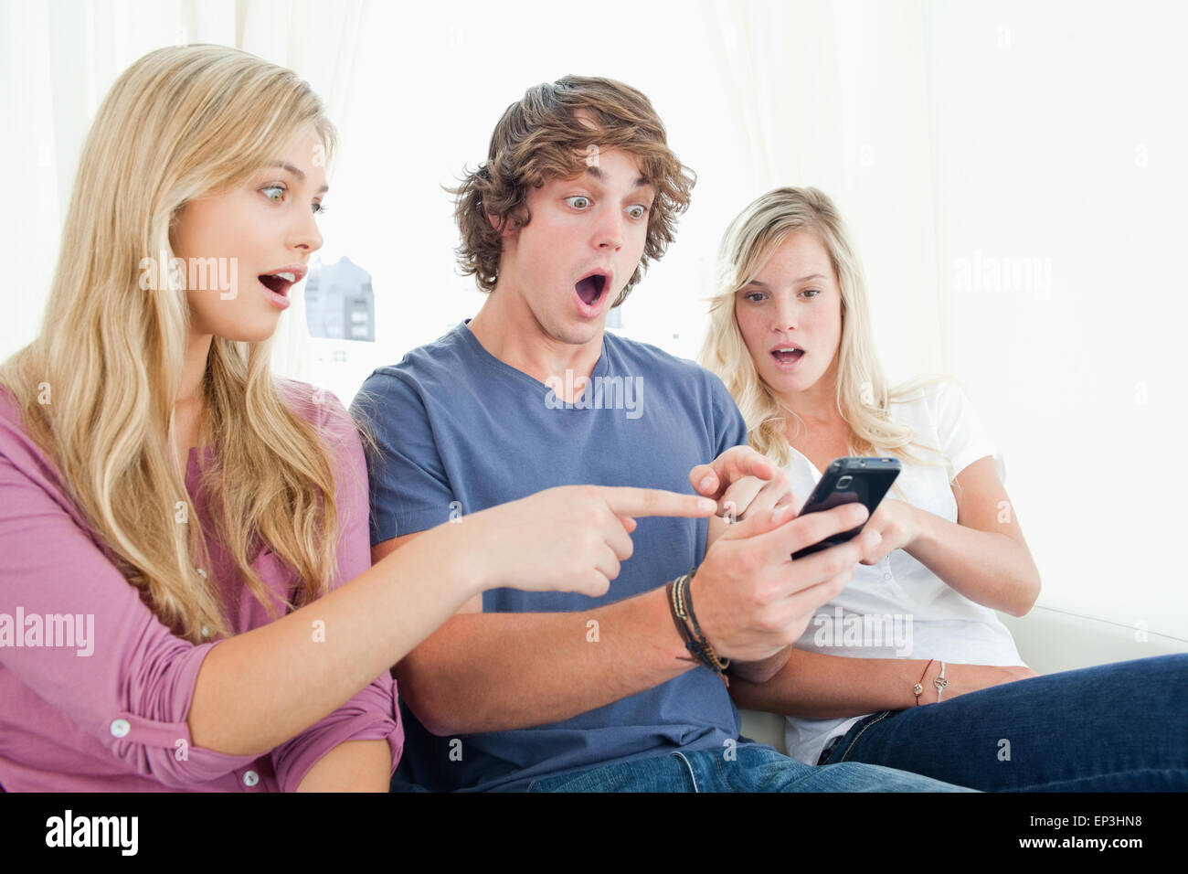Three friends shocked at the message on the phone Stock Photo - Alamy